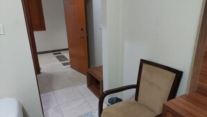 Quarto com porta de madeira, televisão, cadeira e lixeira.