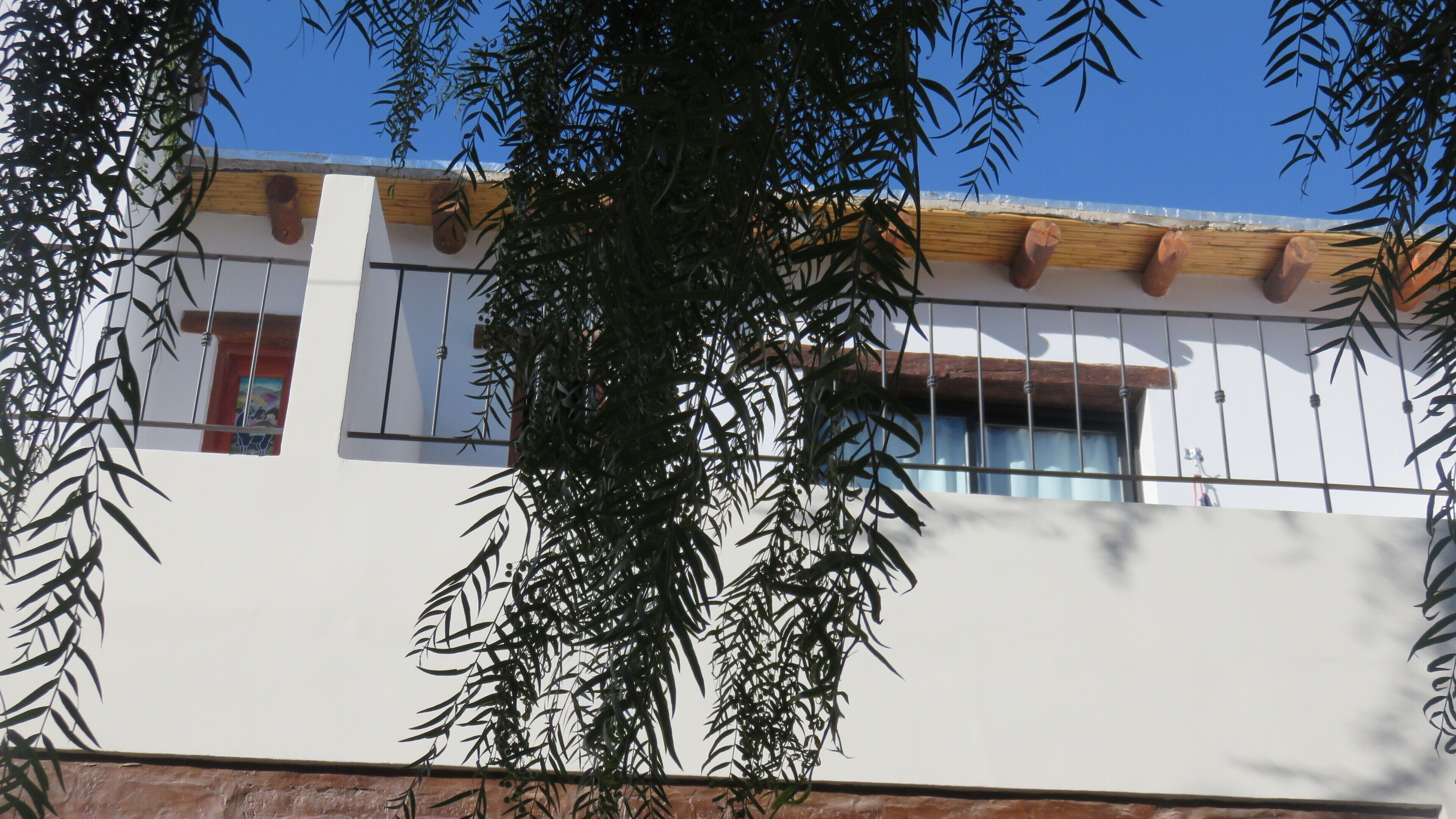 Um edifício com fachada branca, varanda de madeira e janela com grade de metal.
