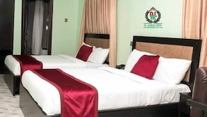 Quarto de hotel com duas camas, cada uma com roupa de cama branca e detalhes vermelhos, cabeceira de madeira e piso de mármore.