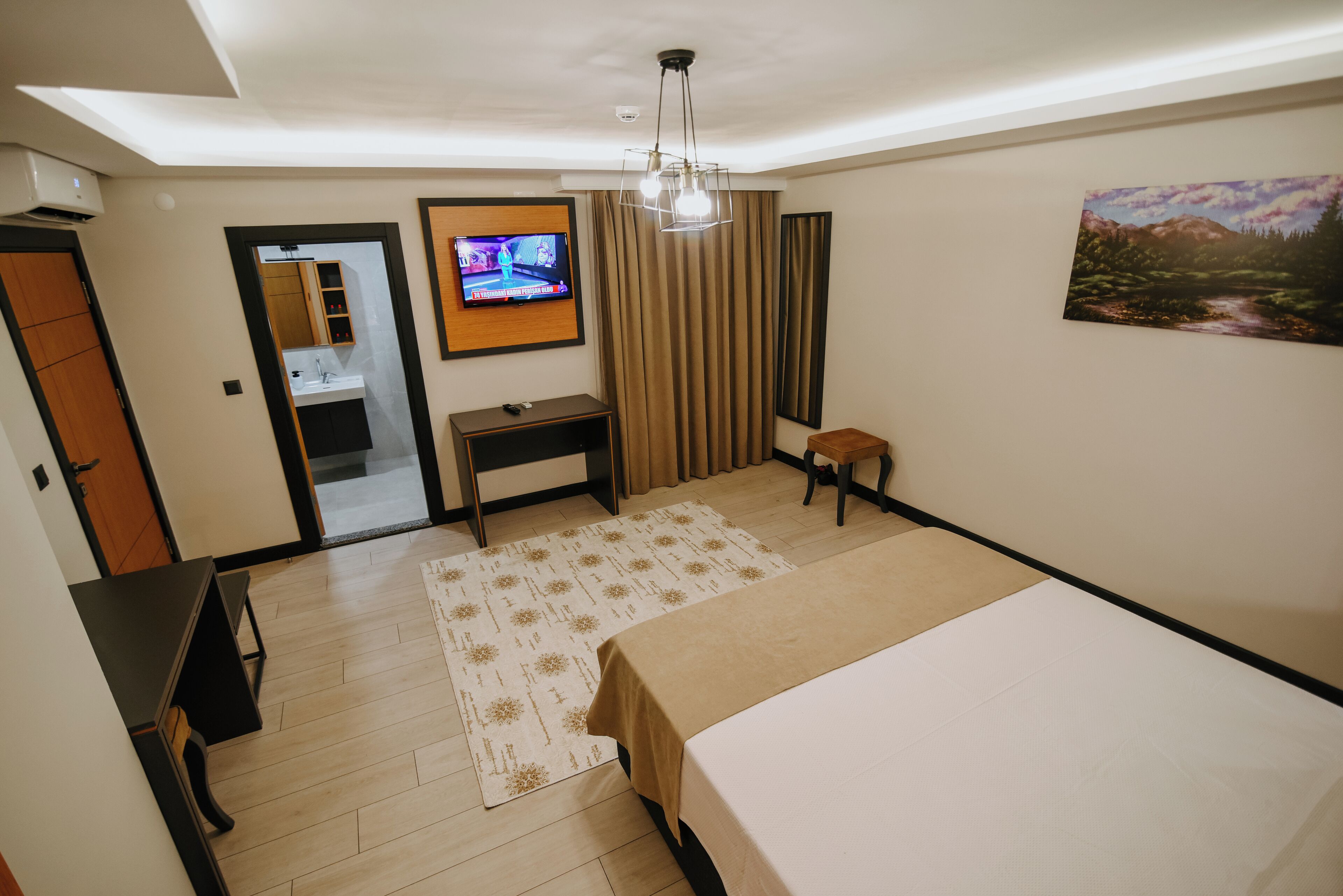 Quarto de hotel com uma cama, uma escrivaninha, uma televisão e um quadro na parede.