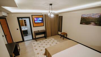 Quarto de hotel com uma cama, uma escrivaninha, uma televisão e um quadro na parede.