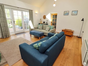 Uma sala de estar com um sofá azul, uma mesa de centro de madeira e uma janela grande com cortinas.