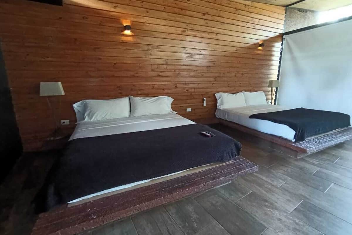 Quarto com duas camas, paredes e piso de madeira, e uma janela com cortina.