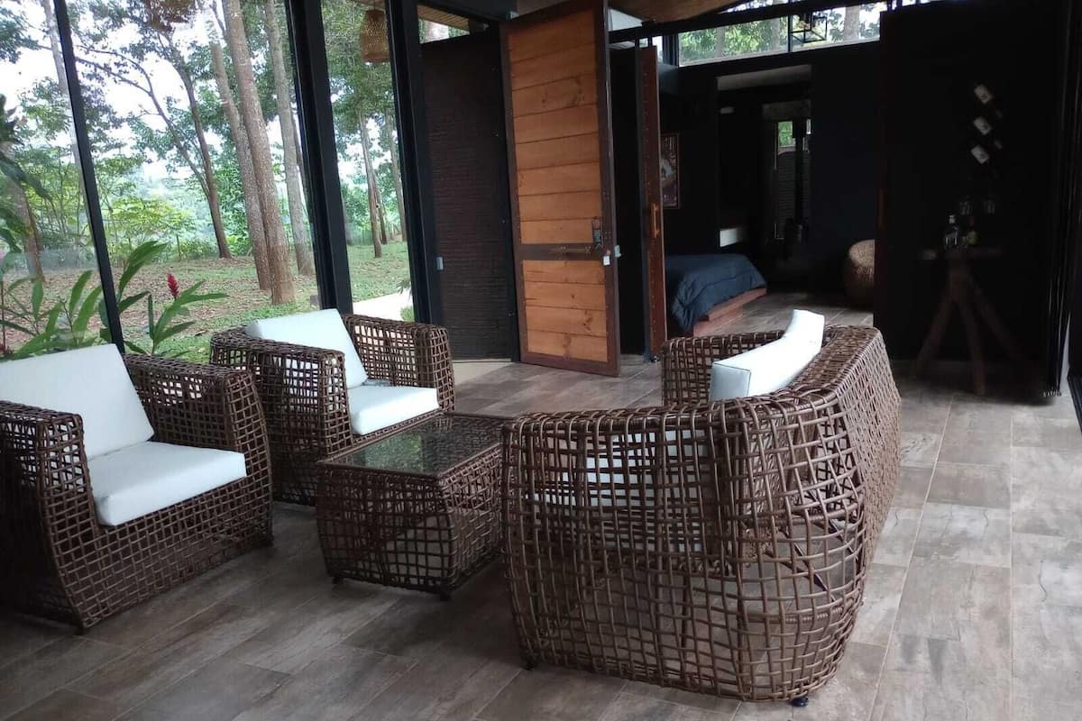 Quarto com móveis de vime, mesa de vidro e vista para o exterior.