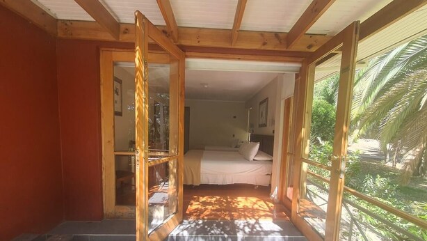 Quarto com cama, janela e vista para o verde lá fora.