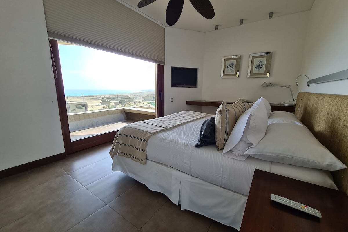 Quarto com cama, mesa de cabeceira, controle remoto e janela com vista para a cidade.