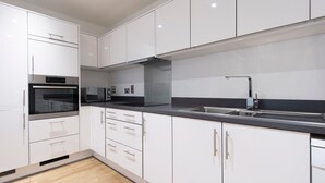 Uma cozinha moderna com armários brancos, um forno de aço inoxidável, um micro-ondas preto e uma pia com torneira.