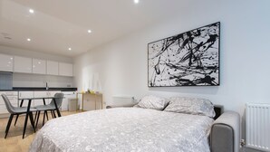 Quarto moderno com cama grande, área de refeições com mesa e cadeiras, e cozinha ao fundo.