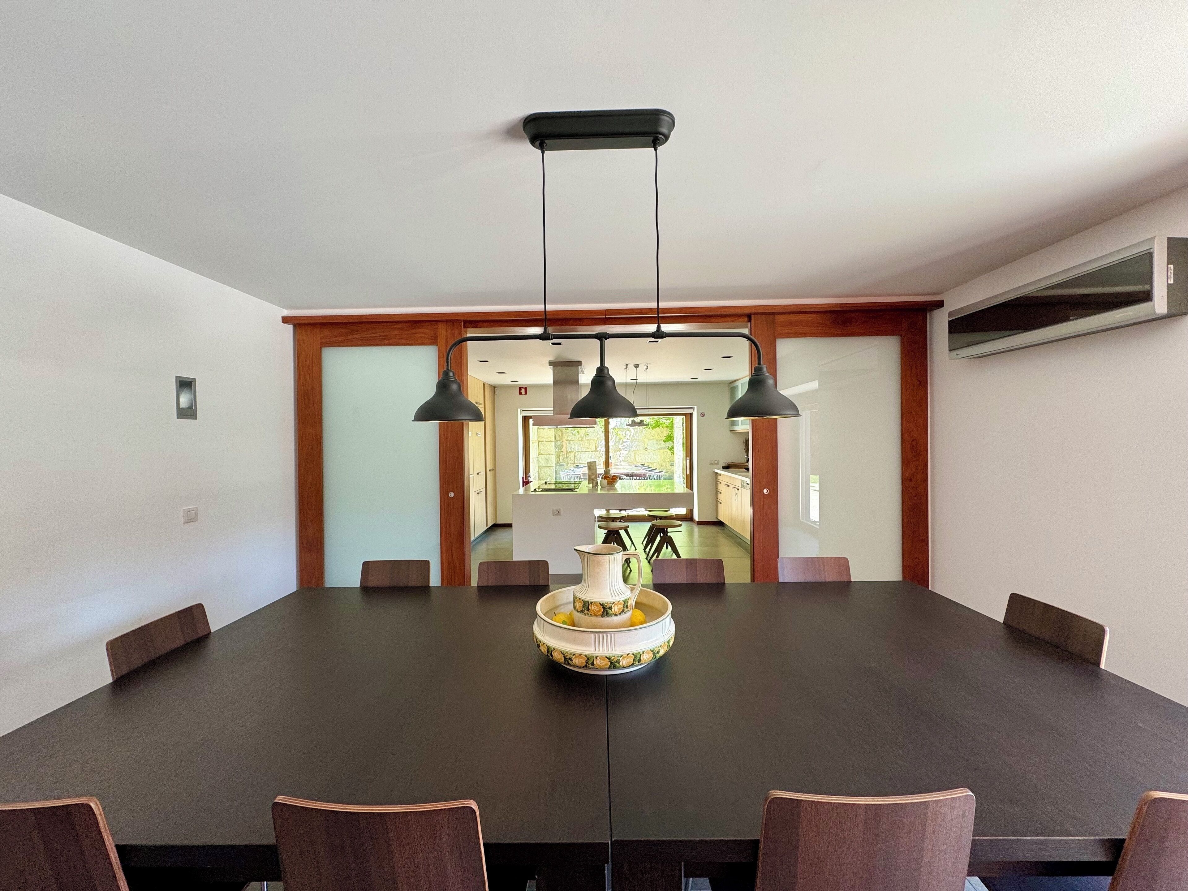 Uma sala de conferências com uma mesa de madeira escura, seis cadeiras e duas luminárias pendentes.