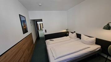 Quarto de hotel com cama, mesa de cabeceira, luminária e um quadro na parede.