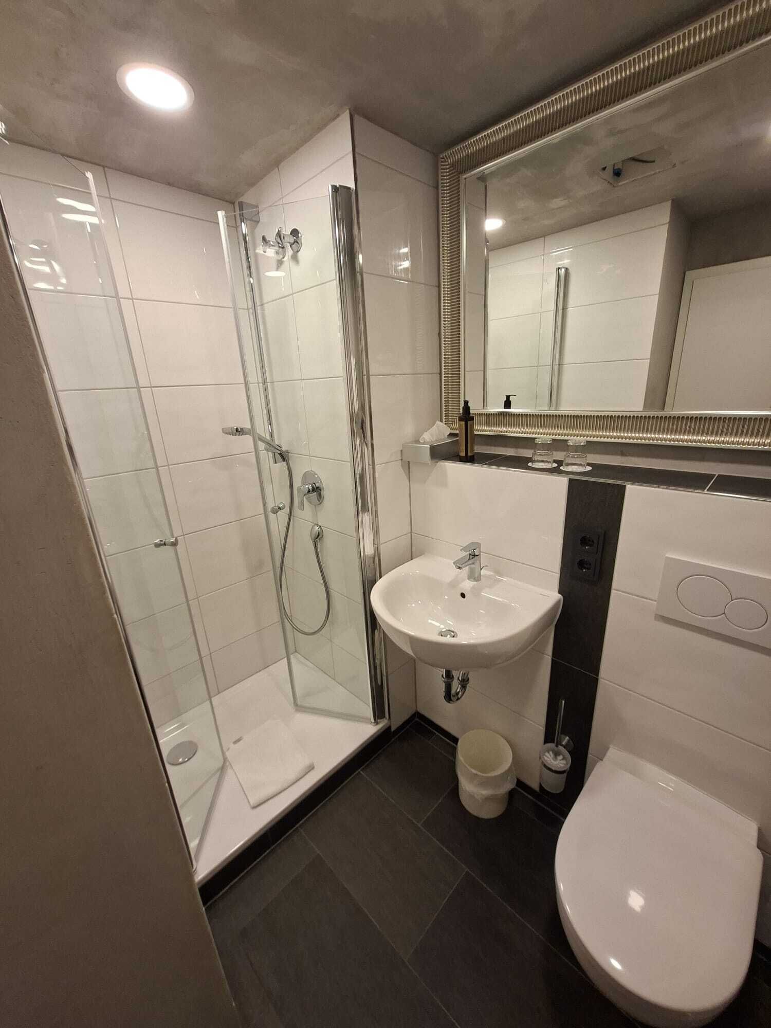 Uma casa de banho moderna com chuveiro em cabine de vidro, lavatório branco e sanita.