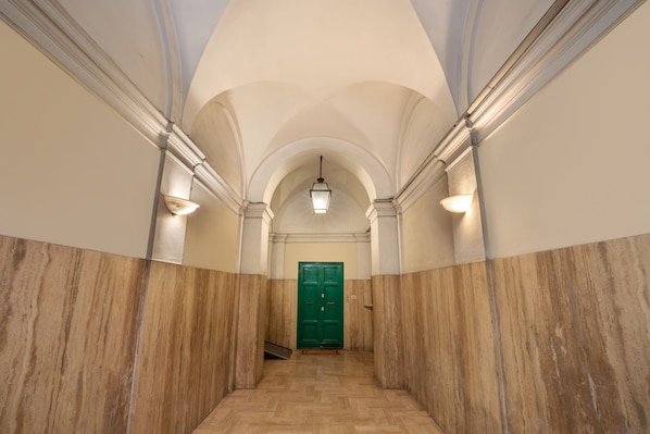 Um corredor com porta verde, paredes de mármore e chão de madeira.