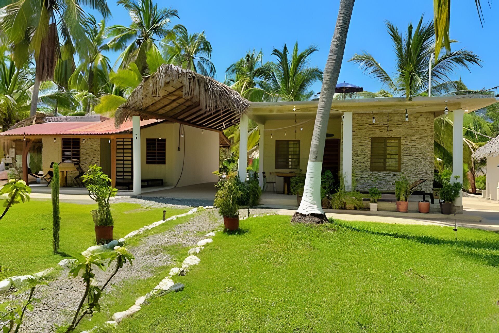 Um resort tropical com estrutura de telhado de palha, um edifício de pedra com colunas e vegetação exuberante.