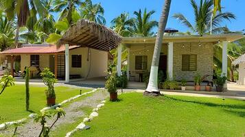 Um resort tropical com estrutura de telhado de palha, um edifício de pedra com colunas e vegetação exuberante.