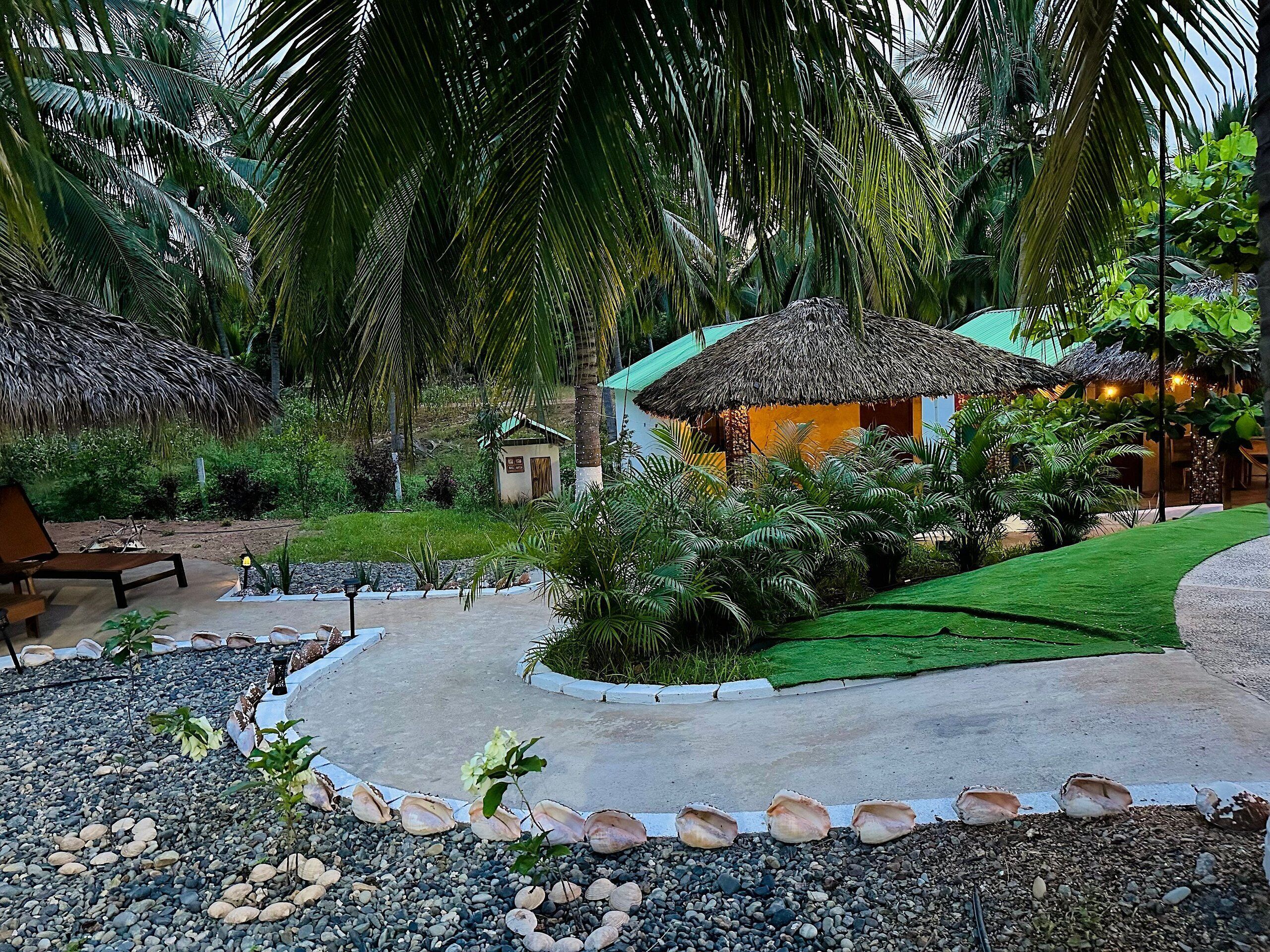 Um resort tropical com cabanas de palha, um caminho pavimentado e vegetação exuberante.