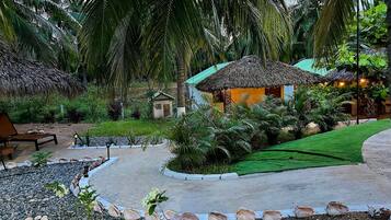 Um resort tropical com cabanas de palha, um caminho pavimentado e vegetação exuberante.