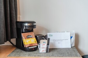 Uma cafeteira, um pacote de café, uma caneca, um porta-guardanapos e um cartão de boas-vindas sobre uma mesa.