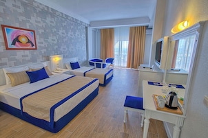 Quarto de hotel com duas camas, uma escrivaninha com espelho, televisão e janela com cortinas.