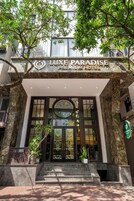 A entrada do Hotel Luxe Paradise Premium, com fachada de pedra, grandes portas de vidro e plantas em vasos.