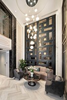 Um lobby moderno com teto alto, painéis decorativos na parede e área de estar central com mesa de centro e dois sofás.
