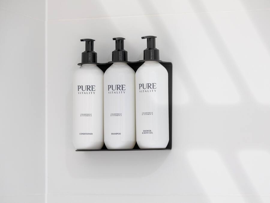 Três frascos de produtos PURE VITALITY: condicionador, shampoo e gel de banho, dispostos sobre uma superfície branca.