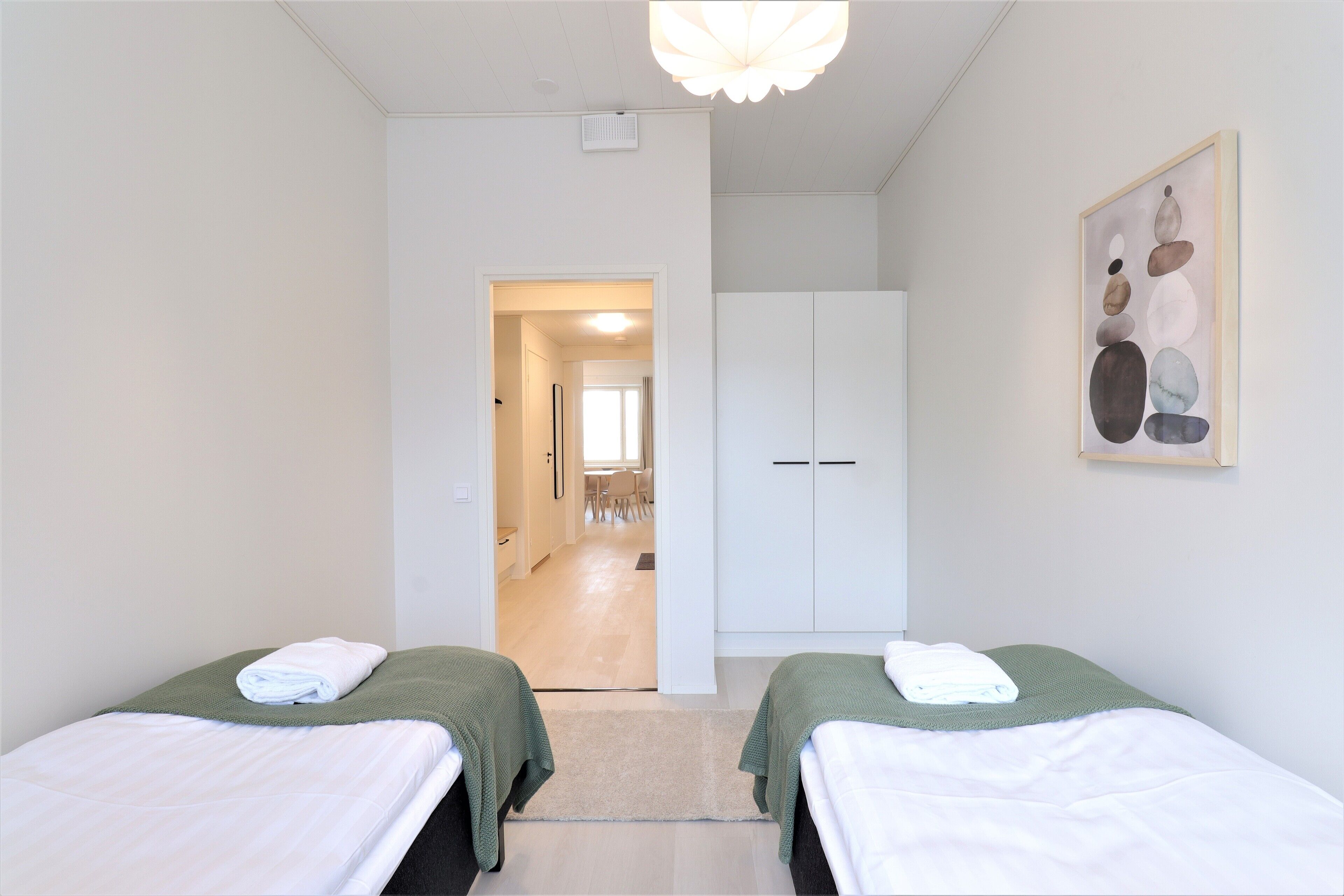 Quarto de hotel com duas camas, um corredor que dá para uma sala de jantar e um guarda-roupa branco.