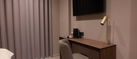 Quarto de hotel com secretária, cadeira, televisão e cortinas.
