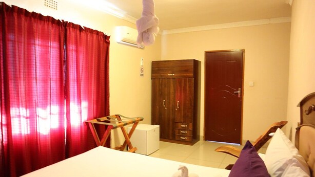 Quarto de hotel com uma cama, escrivaninha, guarda-roupa e cortina vermelha.