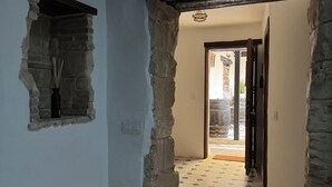 Um corredor estreito com paredes de pedra, chão ladrilhado e uma porta que dá para área externa.