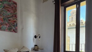 Quarto com uma cama, mesa de cabeceira, pintura na parede e vista de um edifício pela janela.
