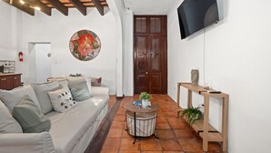 Uma sala de estar com sofá, mesa de centro redonda com uma planta, televisão na parede e porta de madeira.