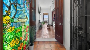 Um corredor com uma janela de vitrais colorida, chão de azulejos e vista para um quarto com cama e janela.