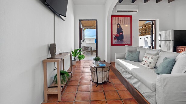 Uma sala de estar moderna com um sofá branco, uma mesinha redonda e uma TV na parede.
