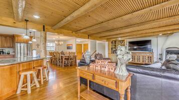 Cozinha ampla com vigas de madeira, área de jantar com lustre e sala de estar com sofá de couro e objetos decorativos.