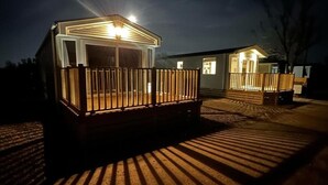 Um pequeno edifício térreo com varanda e área coberta, provavelmente uma cabana ou pousada, iluminado artificialmente à noite.