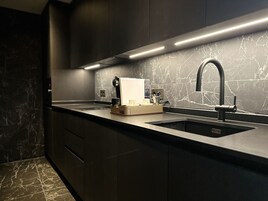Uma cozinha moderna com armários escuros, painel de fundo em mármore e uma pia de aço inoxidável.