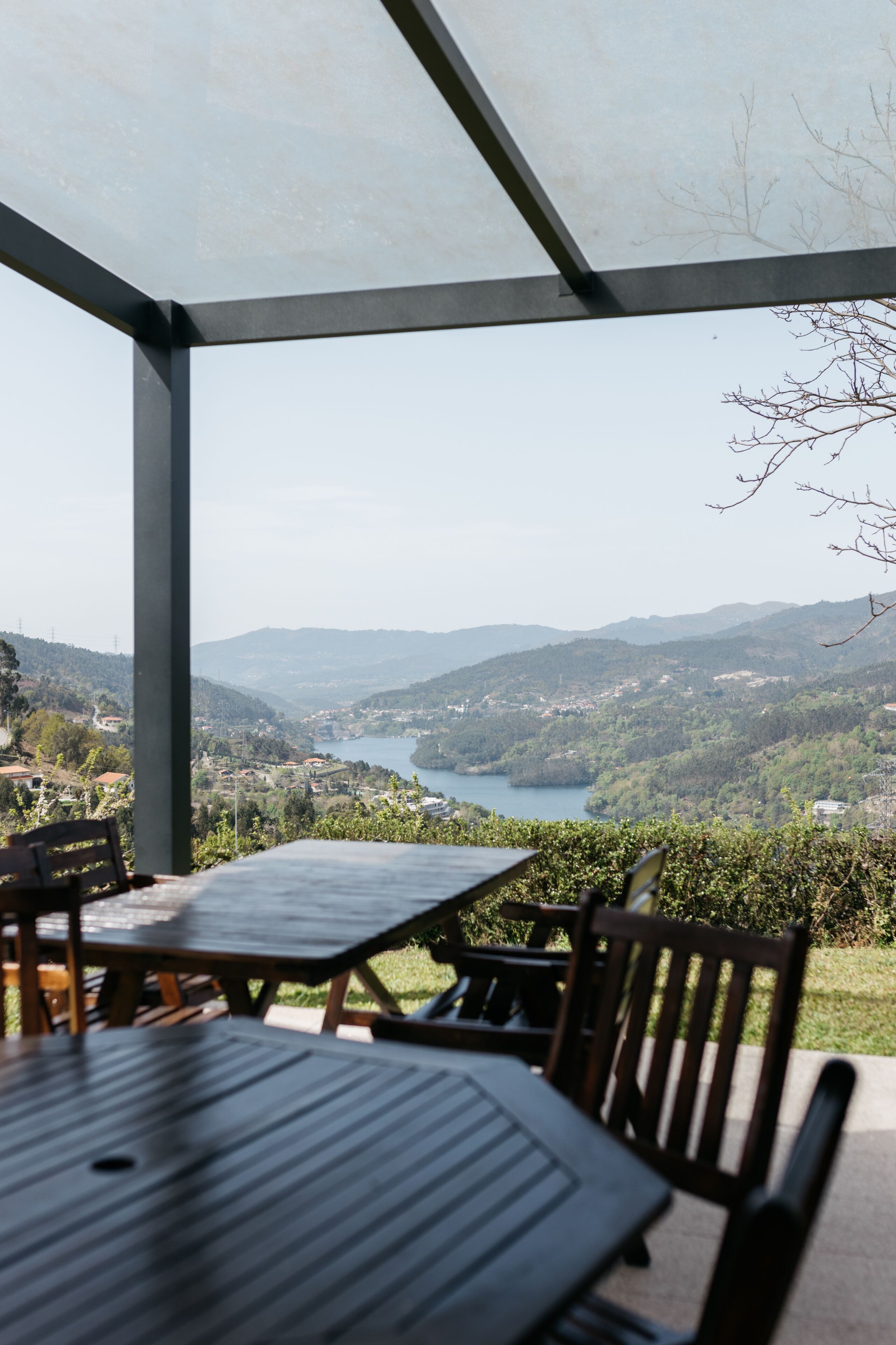 Um pátio externo com mesa e cadeiras, com vista para um vale e lago panorâmicos.