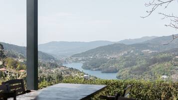 Um pátio externo com mesa e cadeiras, com vista para um vale e lago panorâmicos.