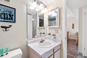 Casa de banho com lavatório branco, um espelho grande e um aviso na parede.