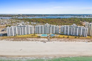 Um hotel à beira-mar com vários edifícios altos, uma piscina central e uma praia arenosa.