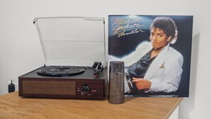 Um toca-discos, um disco de vinil e um cartaz emoldurado de Michael Jackson sobre uma superfície de madeira.
