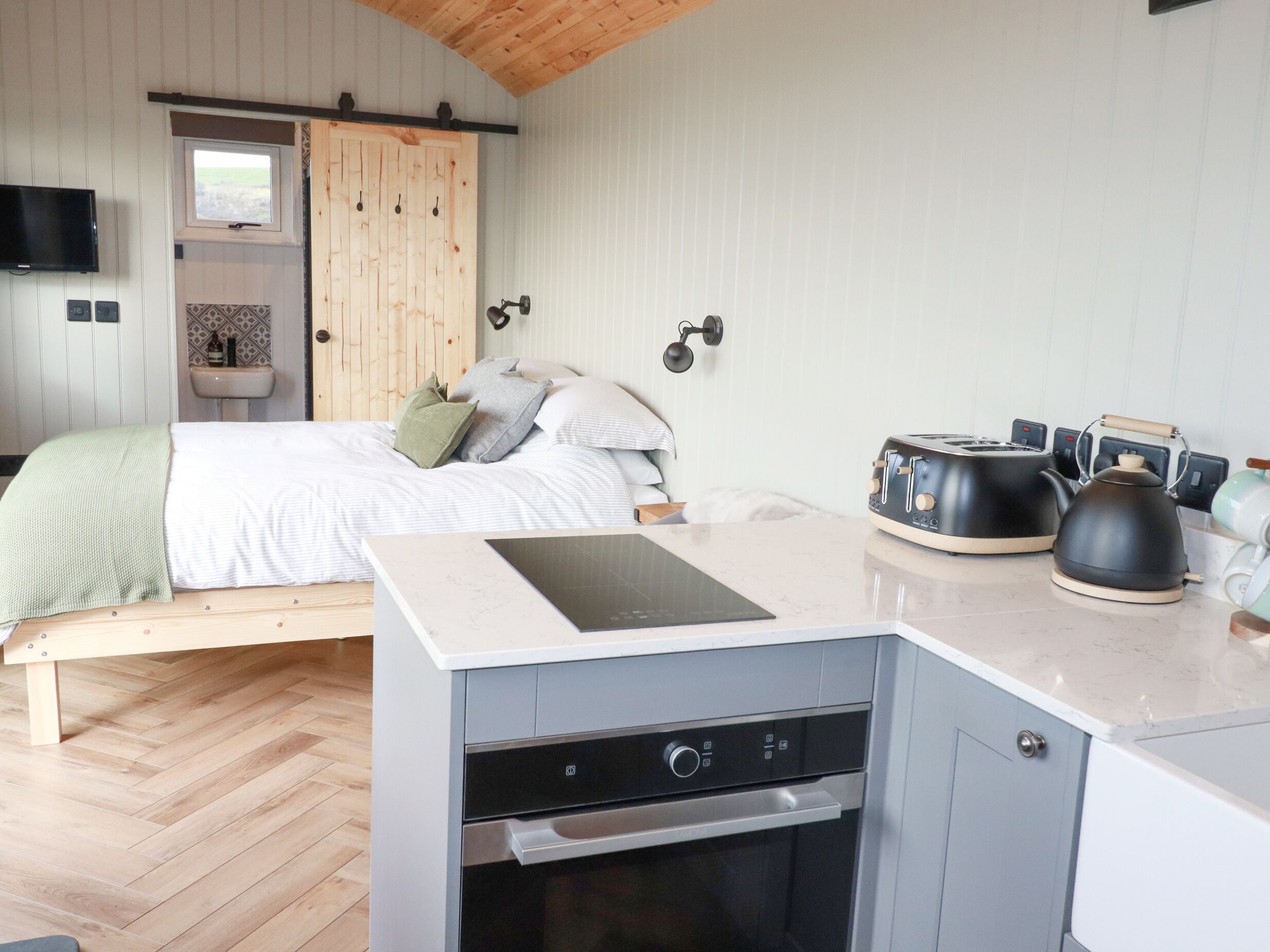 Quarto com cama, mesa de cabeceira, forno embutido e cozinha equipada com chaleira e torradeira.