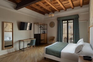 Quarto de hotel com cama, escrivaninha, cadeira, TV e vista para o exterior.