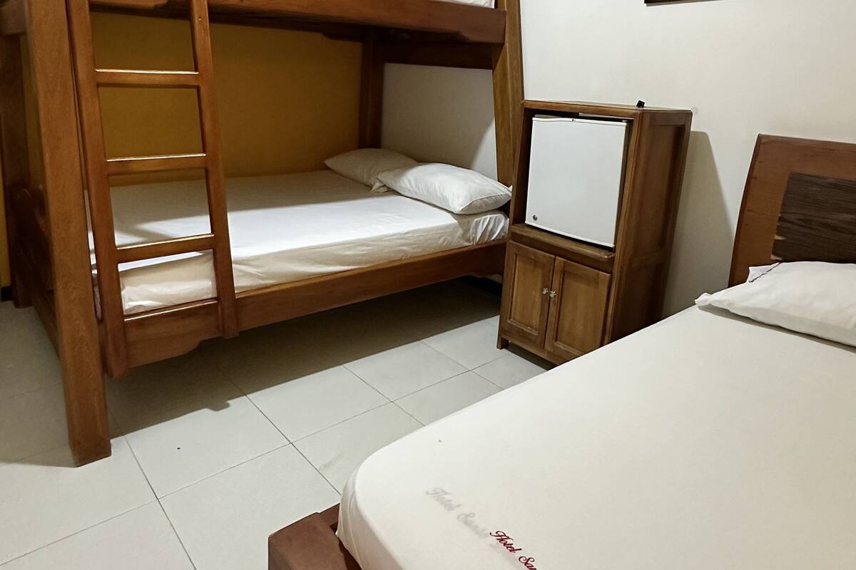 Quarto com beliche, um armário pequeno e uma cama com travesseiro decorativo.
