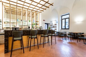 Uma área de bar com teto de madeira, banquetas e prateleiras com garrafas.