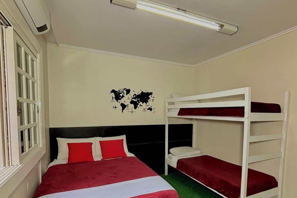 Quarto com cama beliche, uma cama grande com roupa de cama vermelha, adesivo de mapa-múndi na parede e um tapete verde.