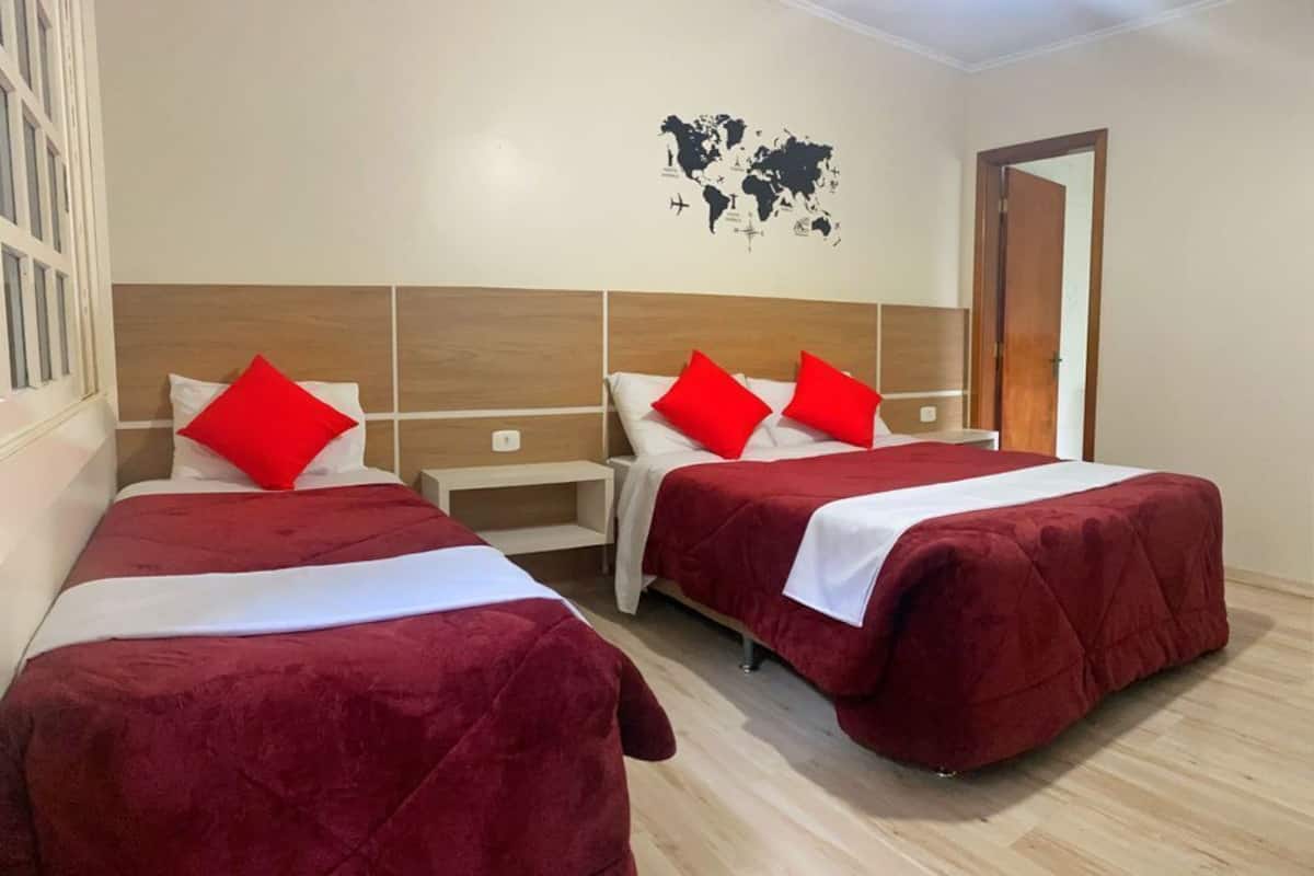 Quarto de hotel com duas camas, cada uma com roupa de cama vermelha e branca, e cabeceira de madeira.