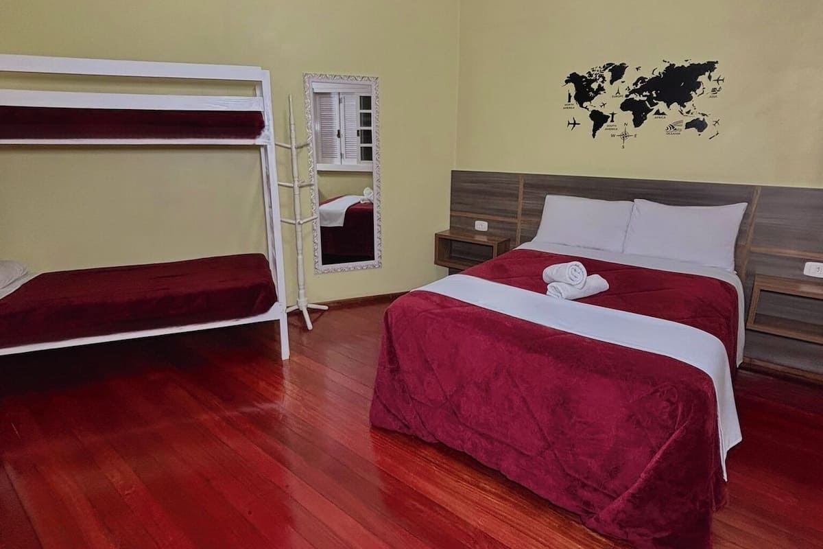 Quarto com duas camas, piso de madeira, mapa-múndi na parede e janela com vista.
