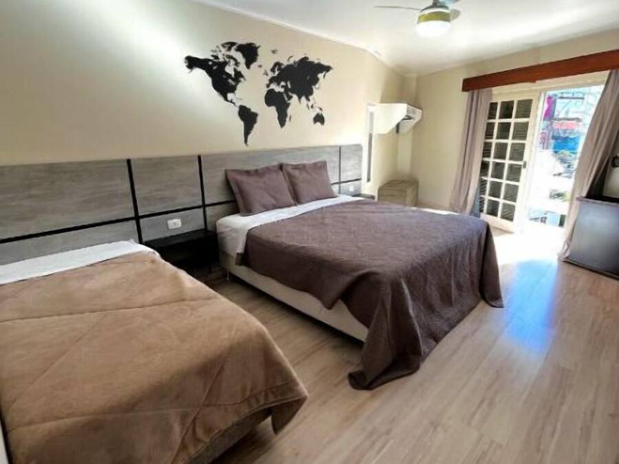 Quarto de hotel com duas camas, um mapa-múndi na parede, um ventilador de teto e vista para o exterior através de uma porta.