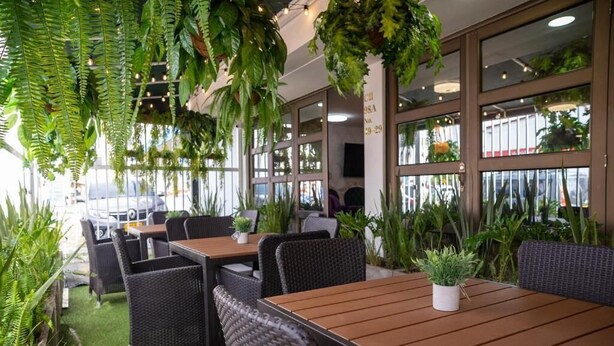 Espaço de estar interno com mesas e cadeiras, rodeado por plantas em vasos e vegetação.